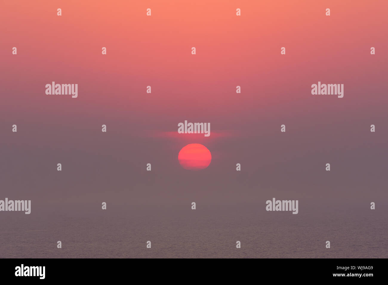 hazy sunset on the sea with big red sun Stock Photo - Alamy