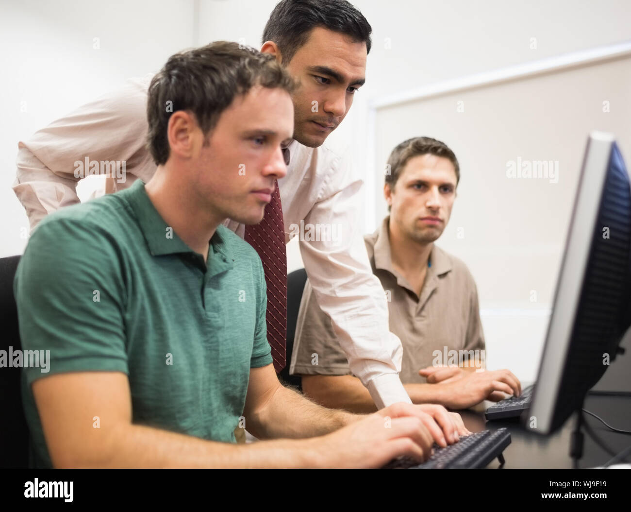 Concentrated teacher with mature students using computer in the ...