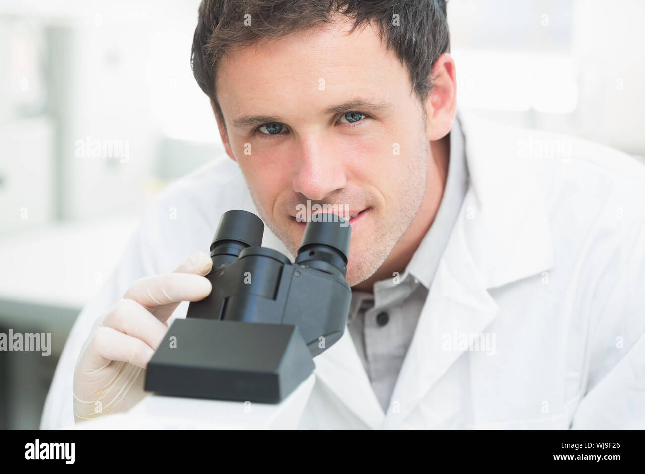 Close-up portrait of a male scientific researcher using microscope in ...