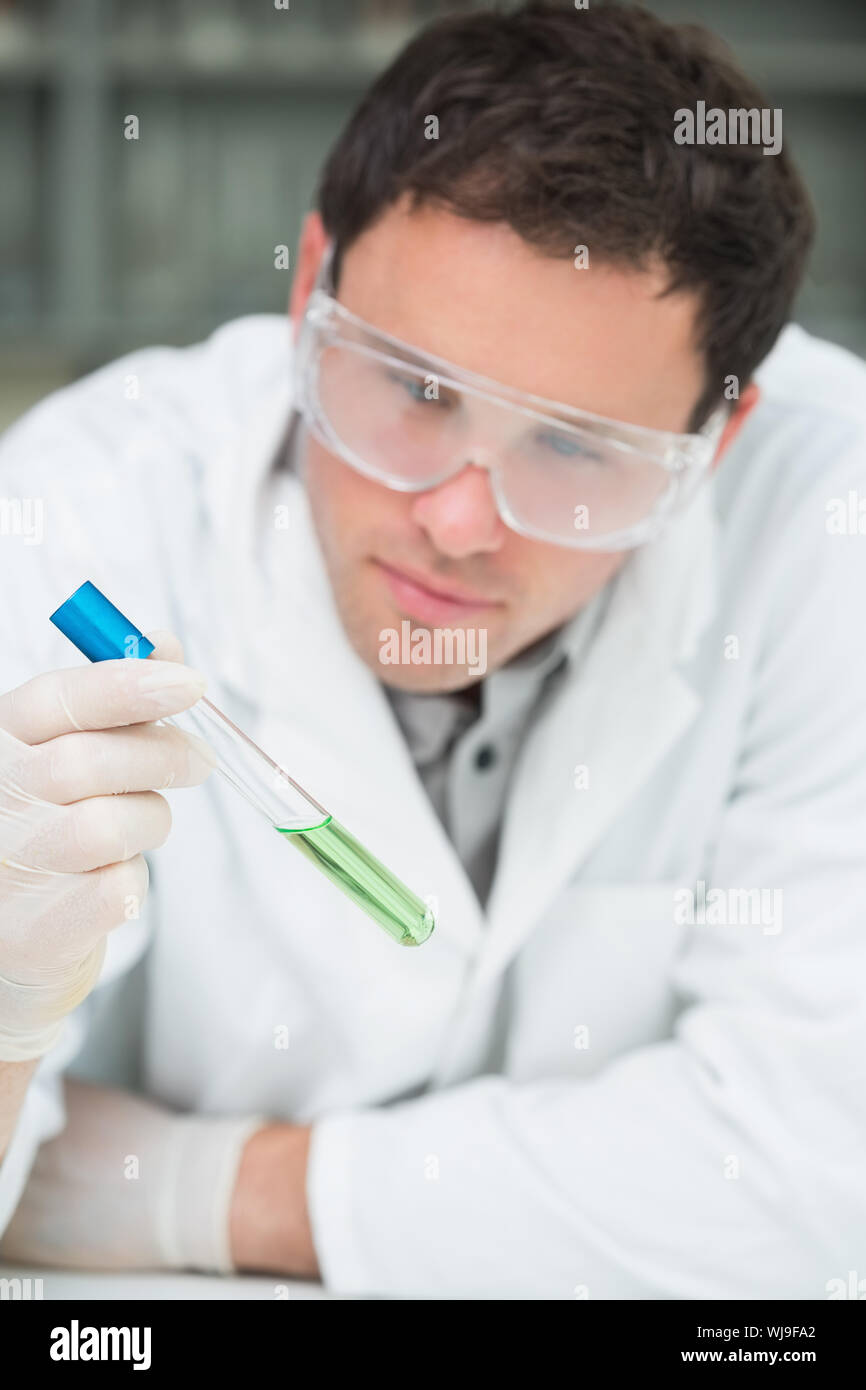 Close-up of a male scientist analyzing green solution in test tube at ...