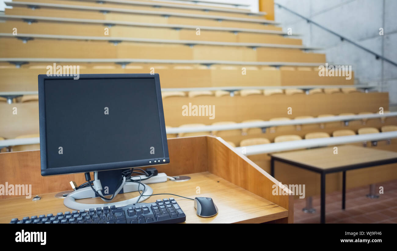 View of computer monitor with empty wooden seats with tables in a ...