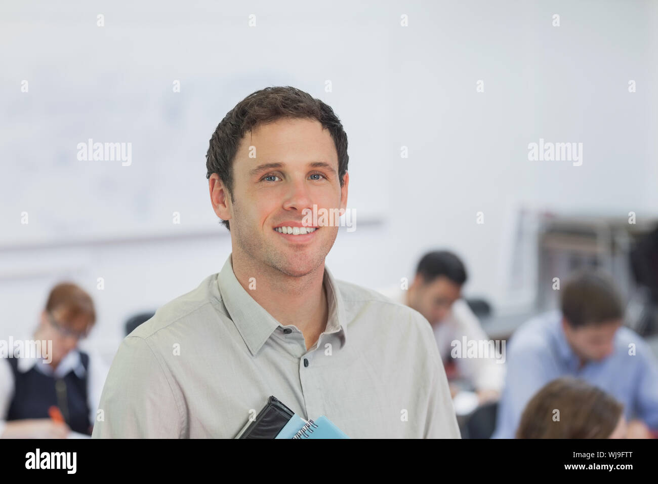 Cute male teacher standing in his classroom smiling at camera Stock ...