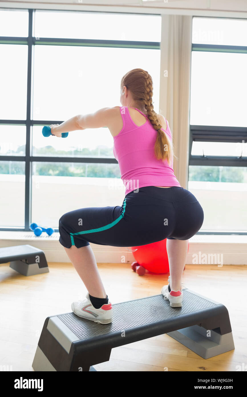 Rear view of a woman performing step aerobics exercise with dumbbells ...