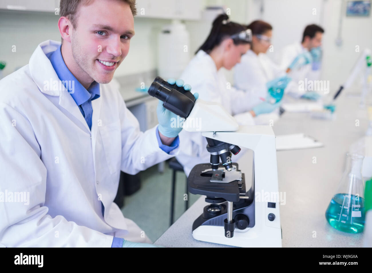 Portrait of a smiling male with researchers working on experiments in ...