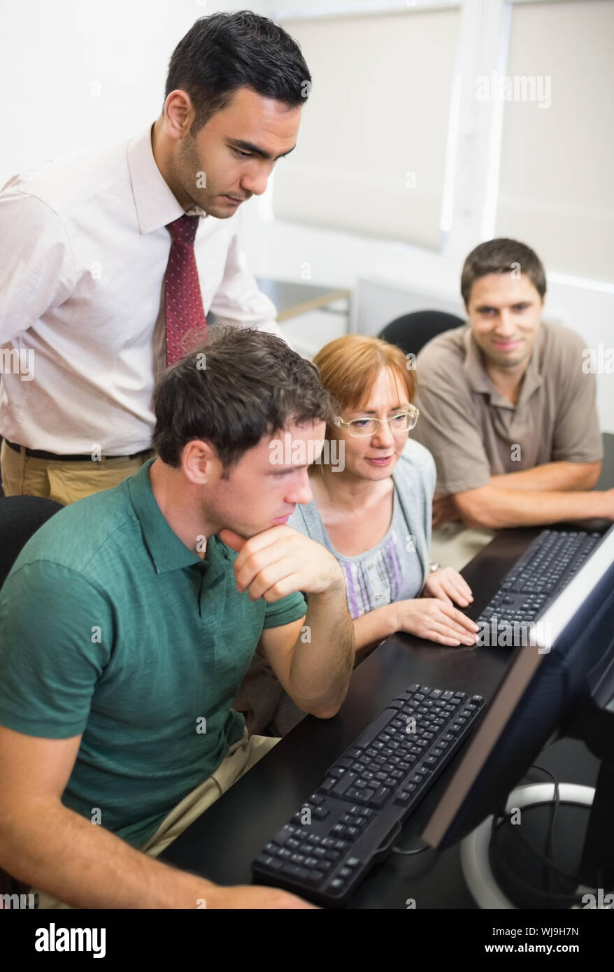 Concentrated teacher looking at mature students use computer in the ...