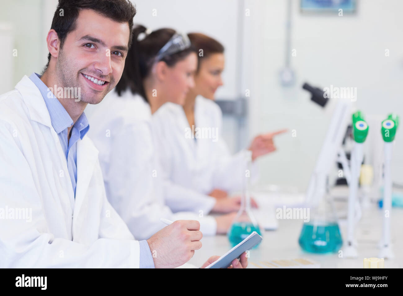 Portrait of a smiling male with researchers working on experiments in ...