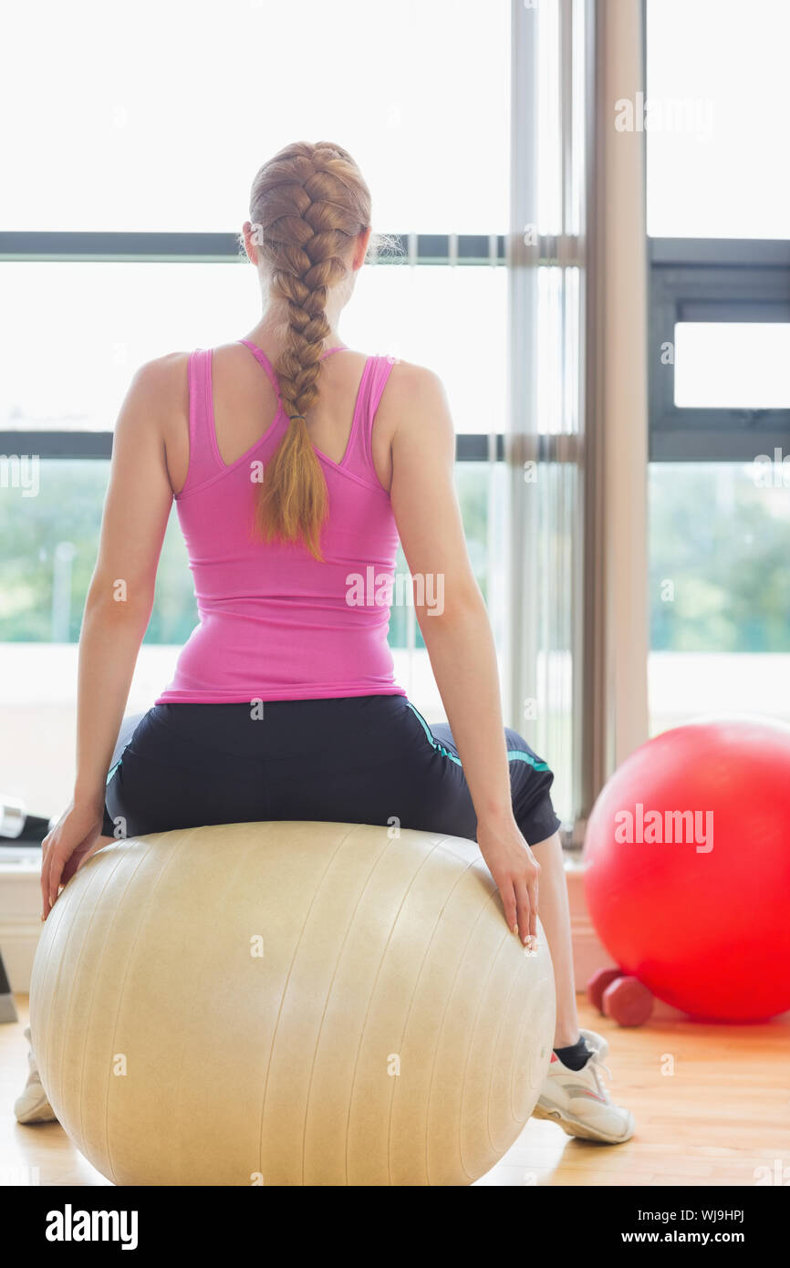Rear view of a fit beautiful young woman sitting on exercise ball in ...