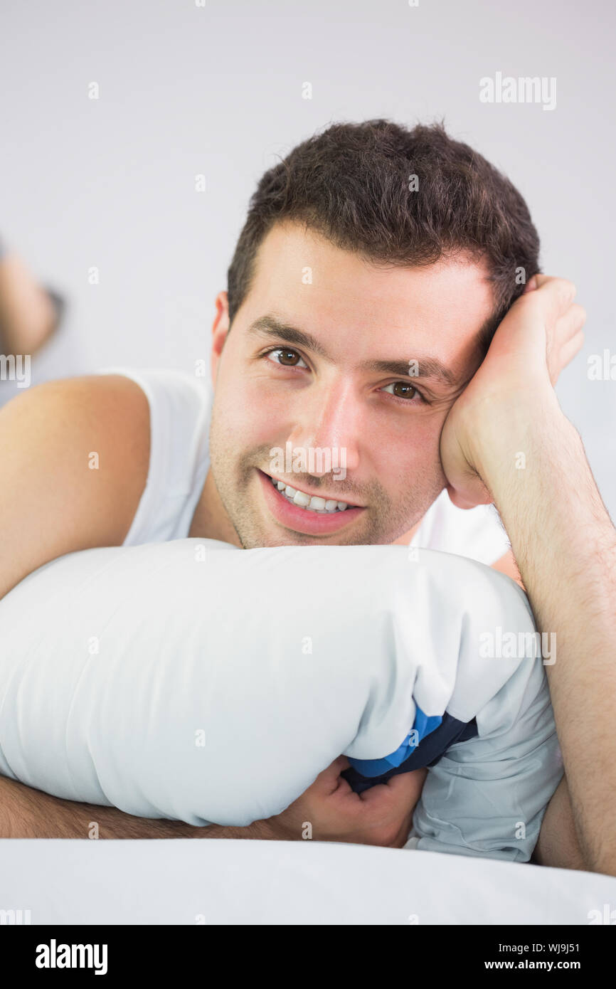 Smiling handsome man lying in bed looking at camera in bright bedroom ...