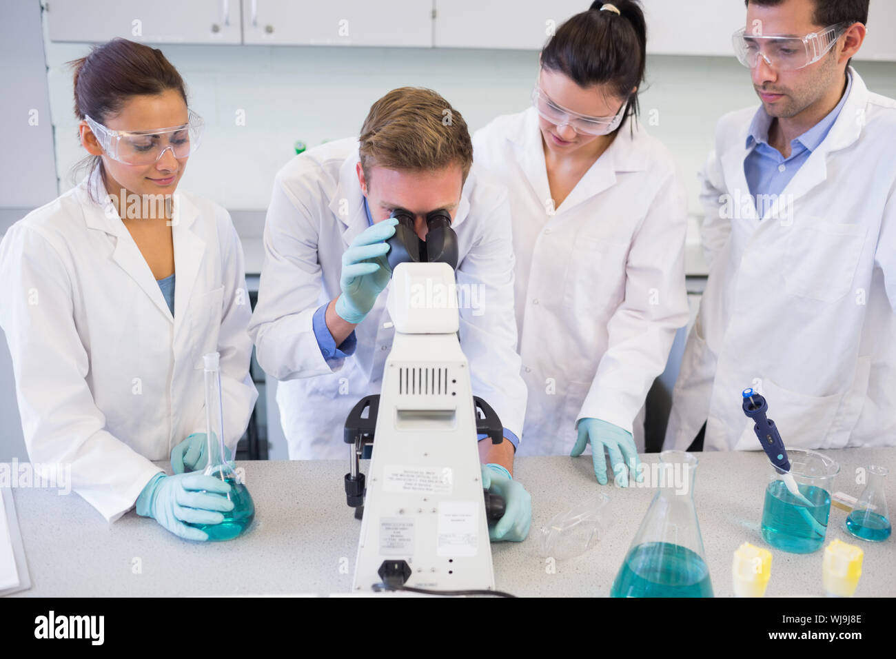 Scientist using microscope with others besides him in the laboratory ...