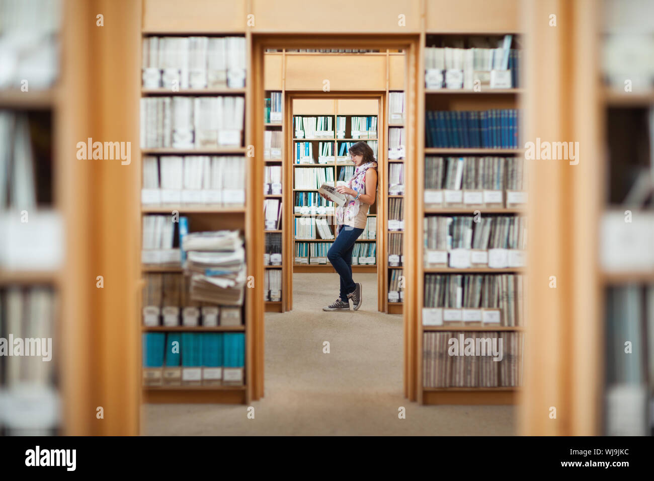 Full length side view of a female student reading a book in the library ...