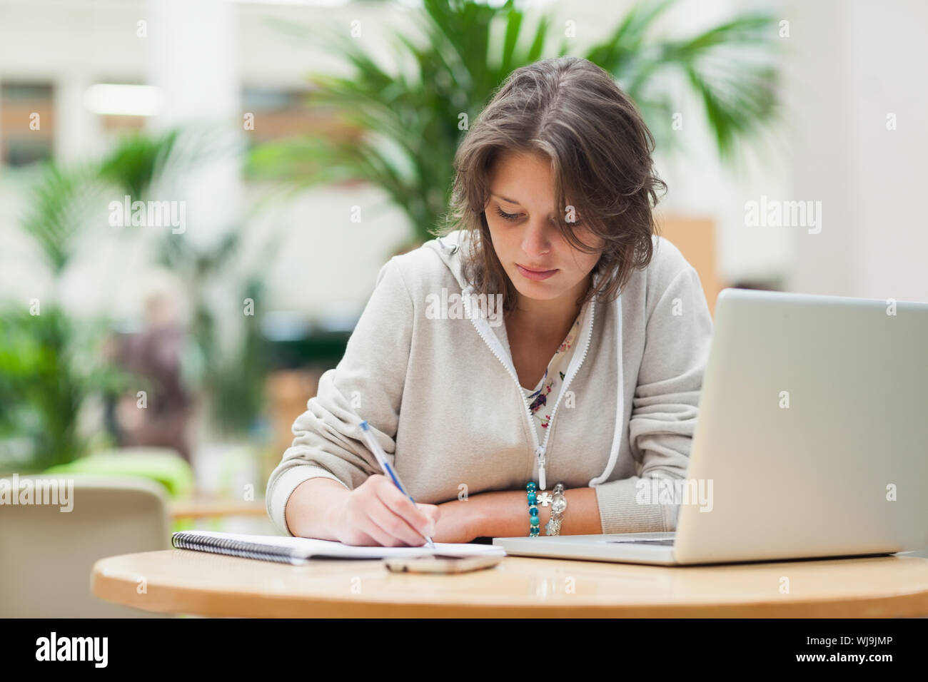 Concentrated female student doing homework by laptop at cafeteria table ...