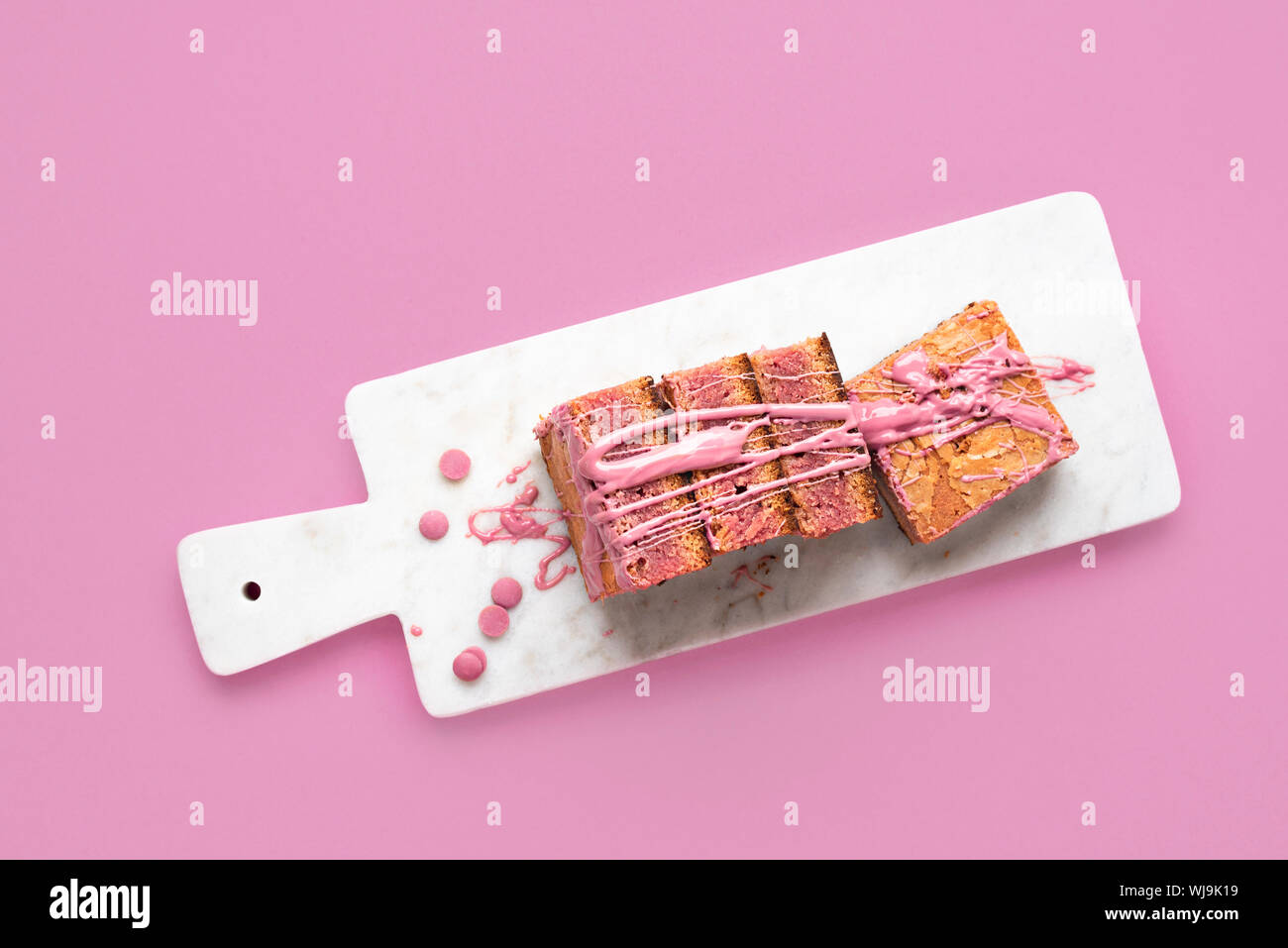 Ruby chocolate brownies on marble cutting board and pink background. Above view of pink ...