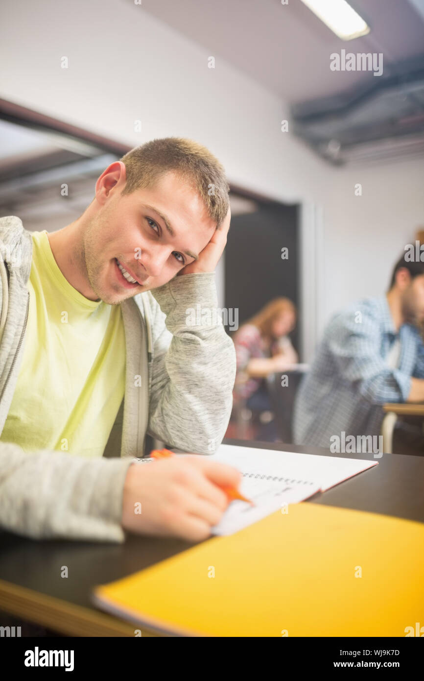 Portrait of a smiling male student with others writing notes in the ...