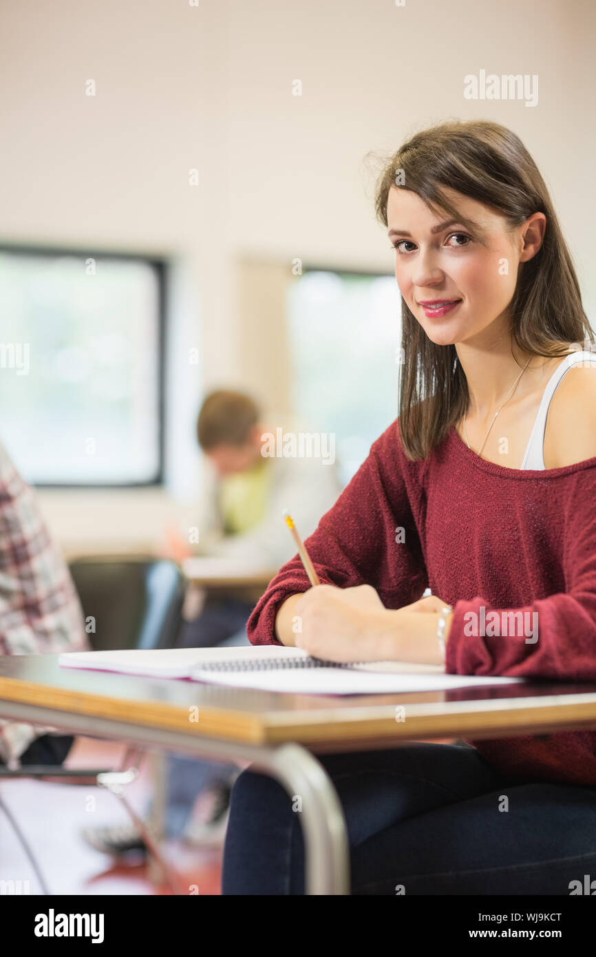 Portrait of a smiling female student with others writing notes in the ...