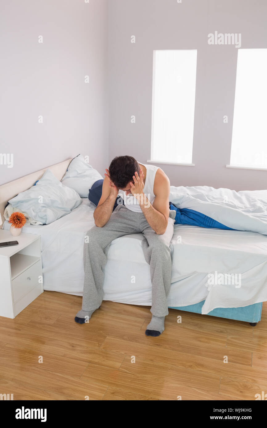 Sleepy casual man sitting on bed in bright bedroom Stock Photo - Alamy