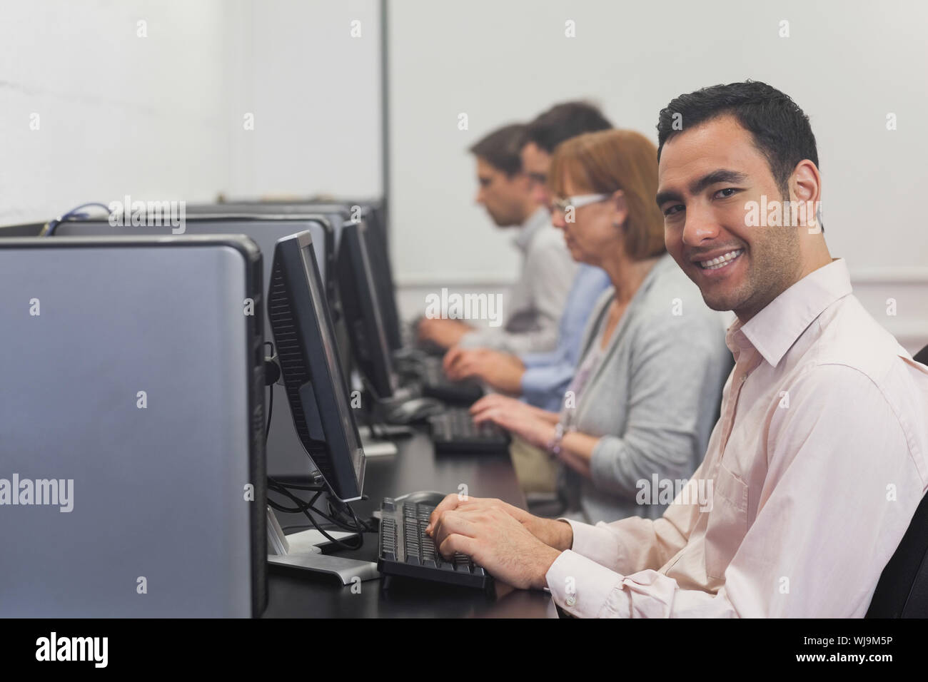 Cheerful mature student sitting in computer class smiling at camera ...