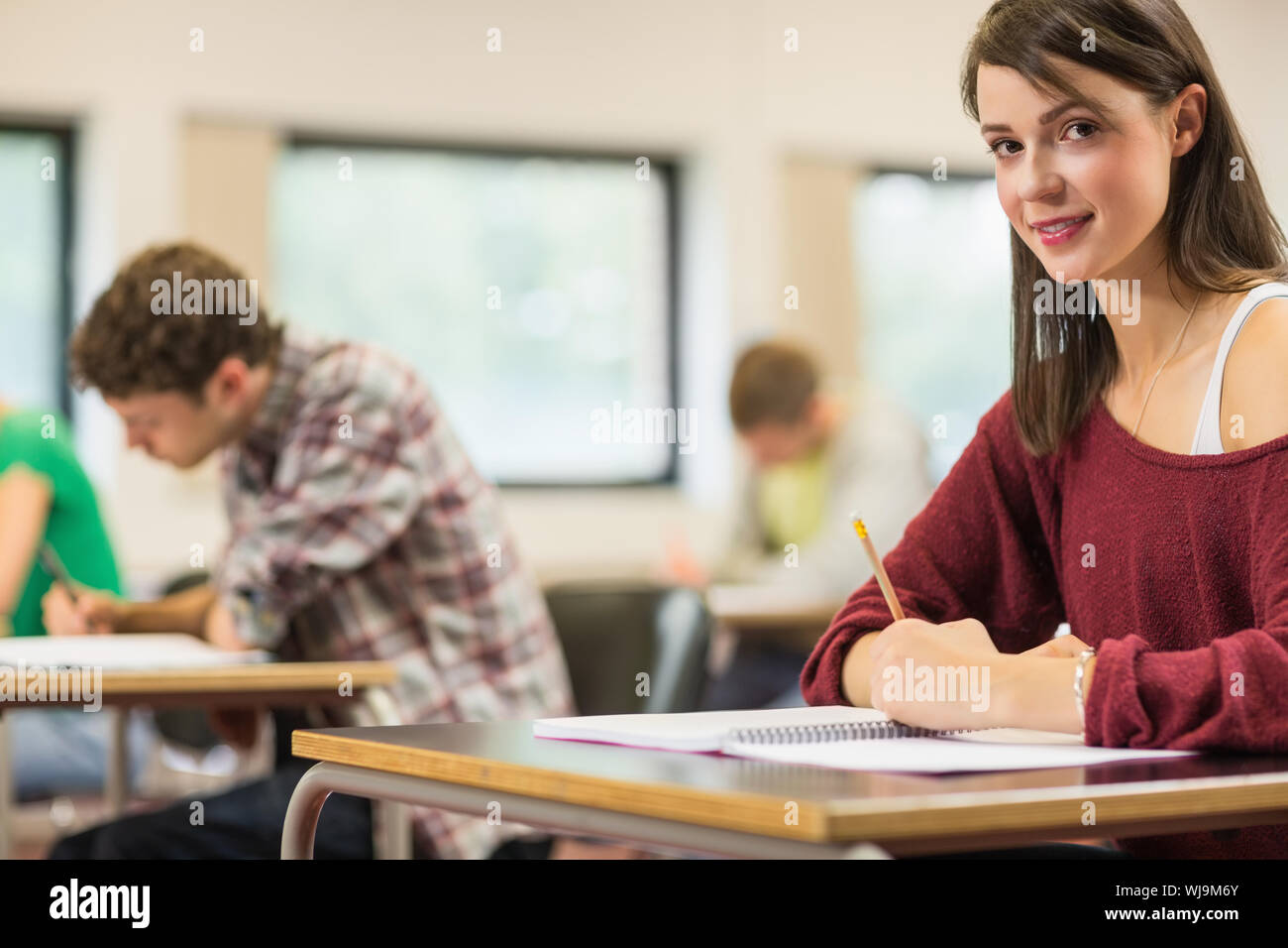 Portrait of a smiling female student with others writing notes in the ...
