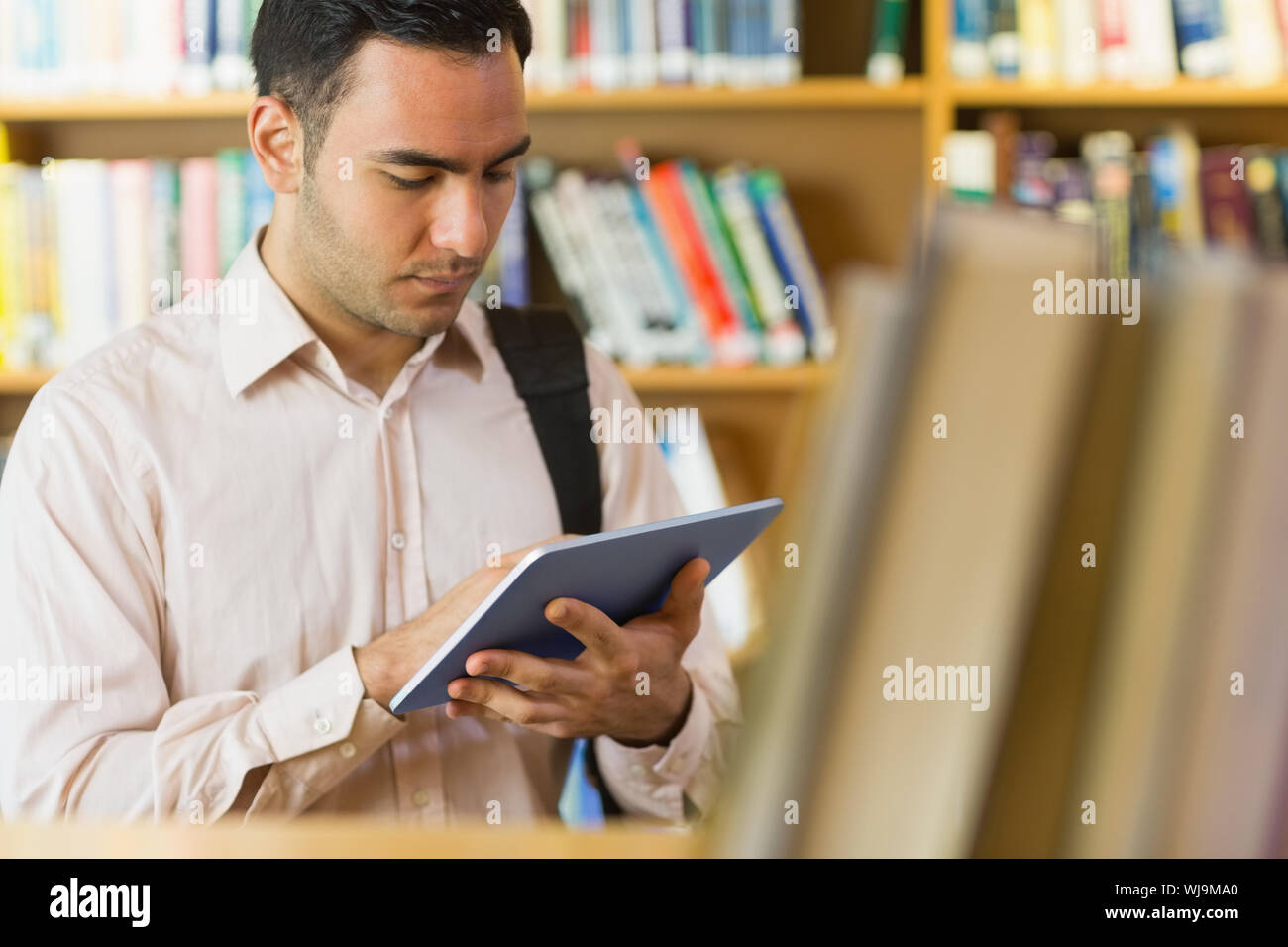 Concentrated mature student using tablet PC against bookshelf in the ...