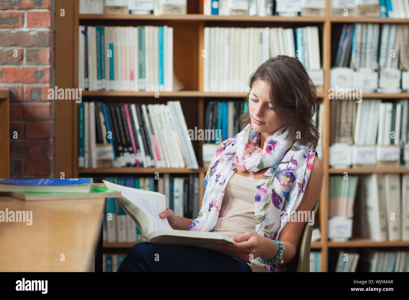 Female student sitting on chair and reading a book in the library Stock ...