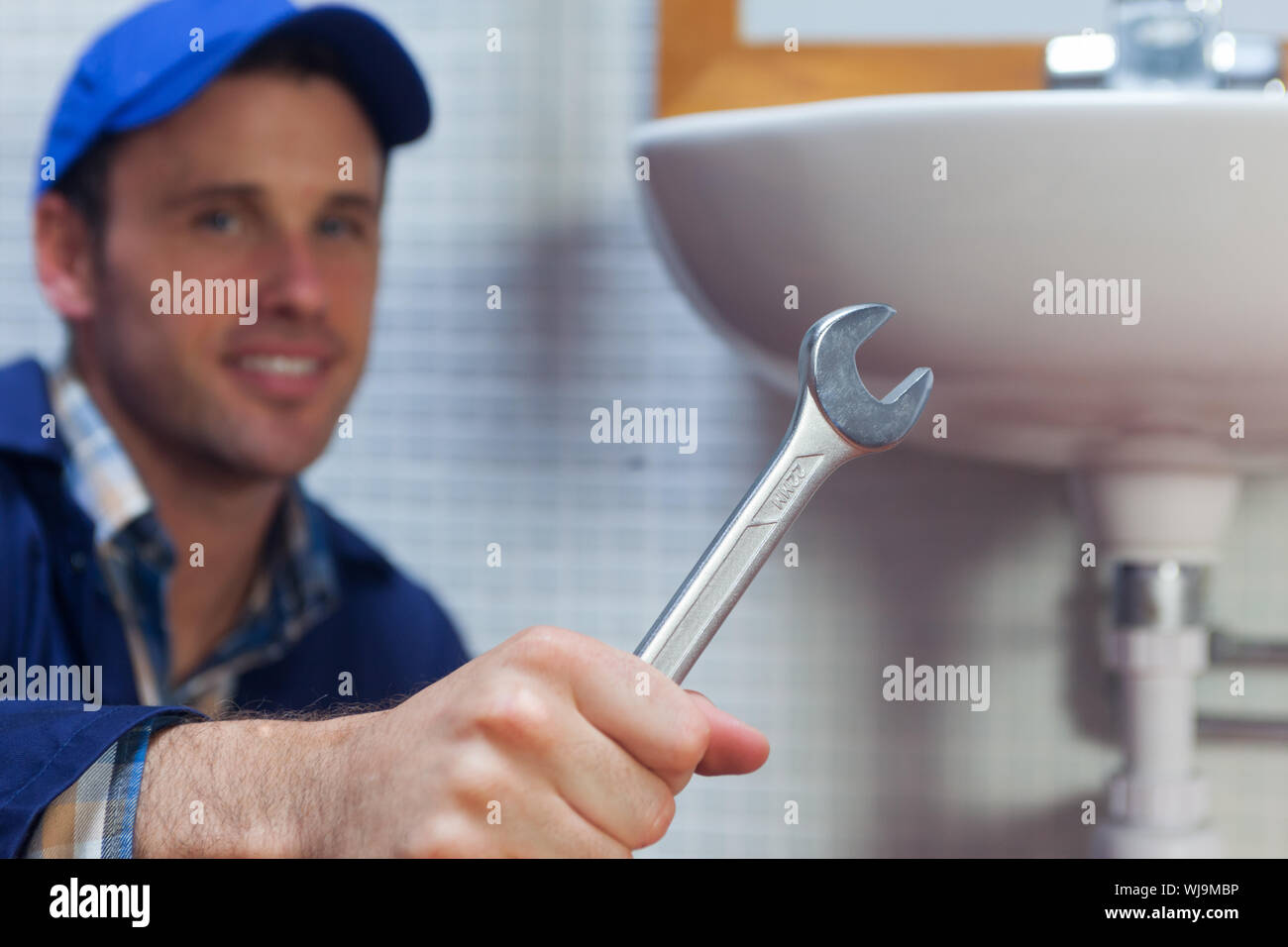 Handsome cheerful plumber showing wrench in public bathroom Stock Photo ...