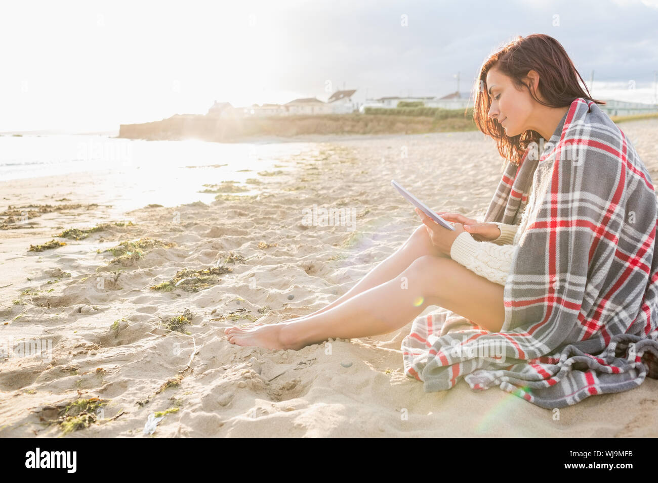Side view of a young woman covered with blanket using tablet PC at the ...