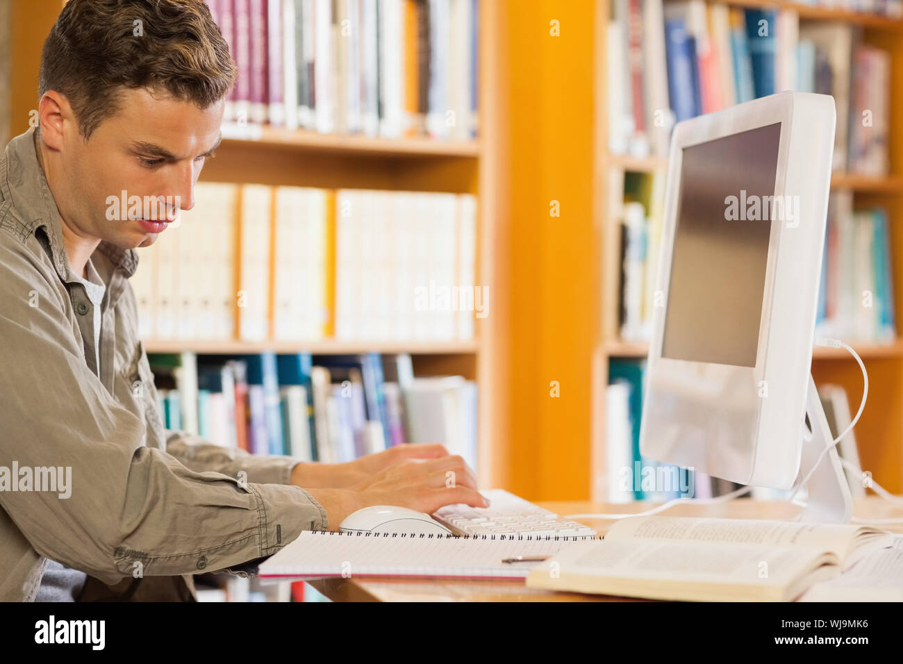 Handsome serious student using computer reading notes in library Stock ...