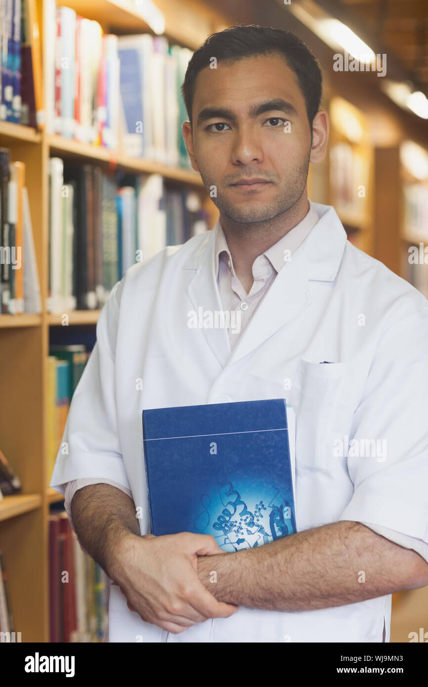 Serious intellectual man posing in library with a book looking at ...