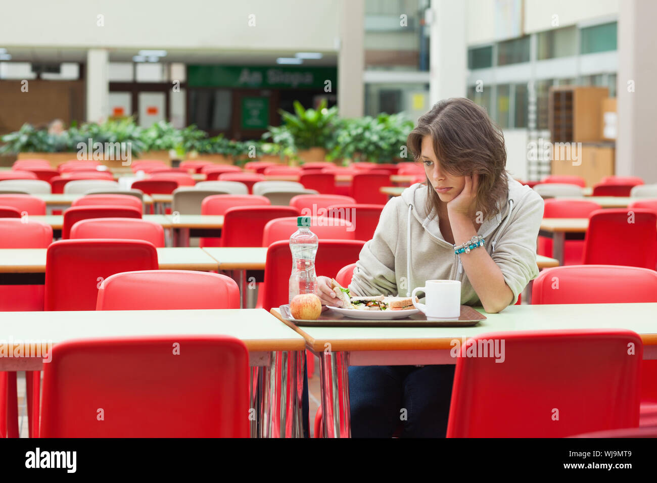 Alone and sad female student sitting in the cafeteria with food tray ...