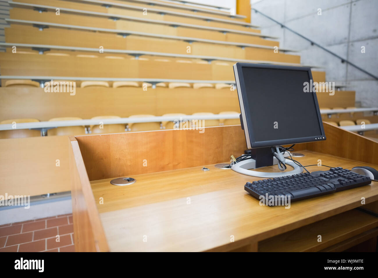 View of computer monitor with empty wooden seats with tables in a ...