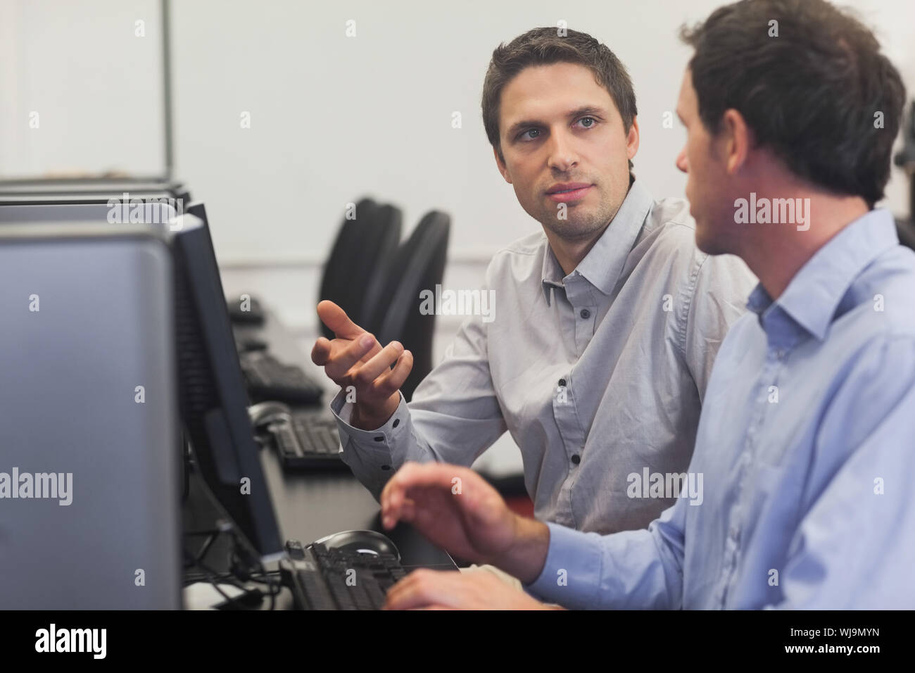 Two handsome men talking while sitting in computer class pointing at ...