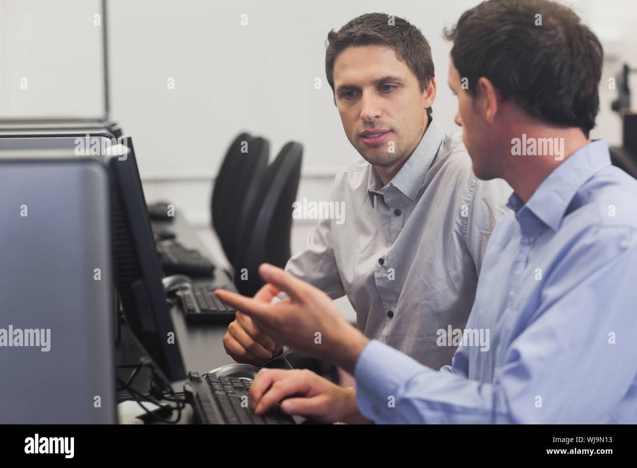 Two attractive men talking in computer class pointing at monitor Stock ...