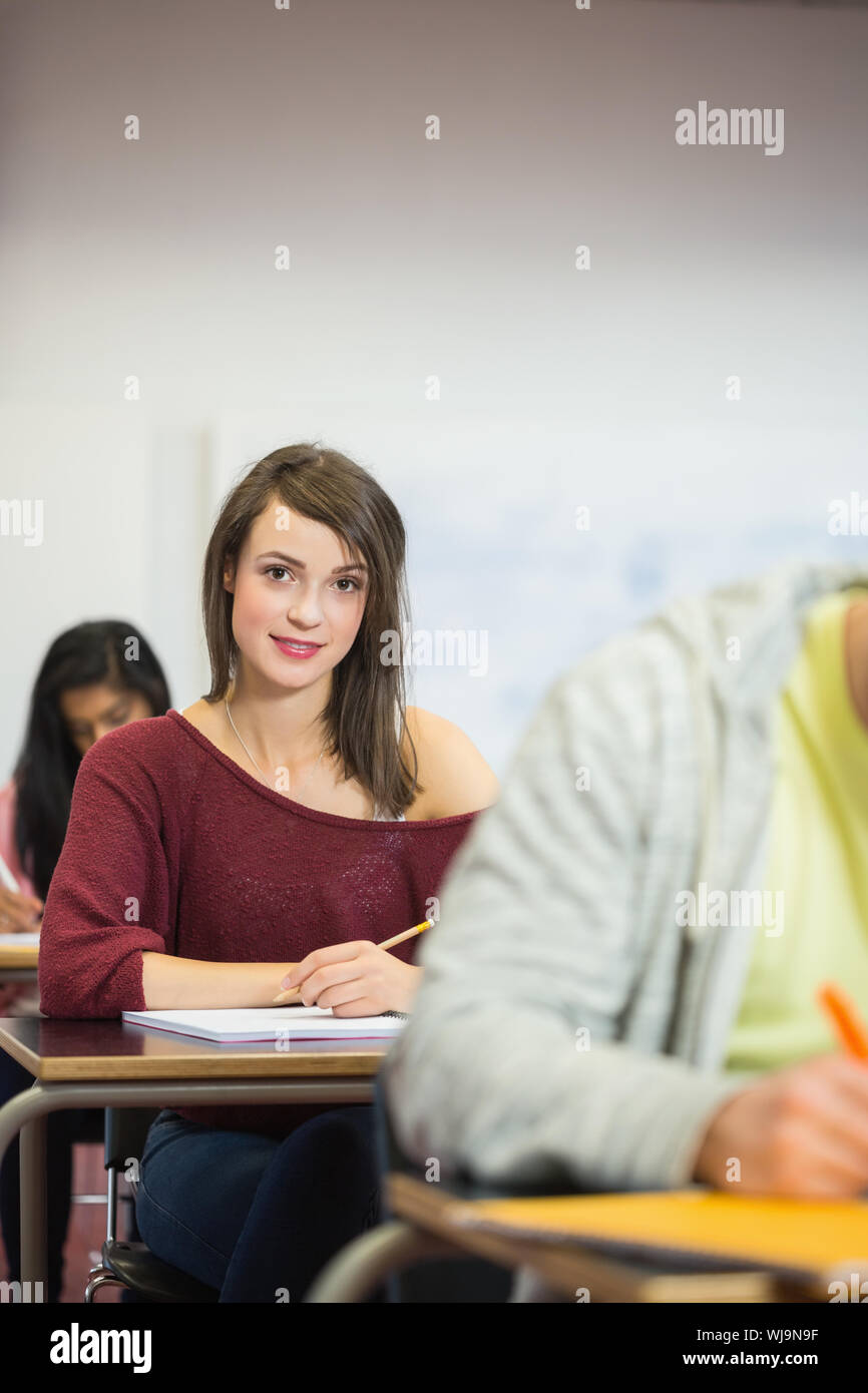 Portrait of a smiling female student with others writing notes in the ...