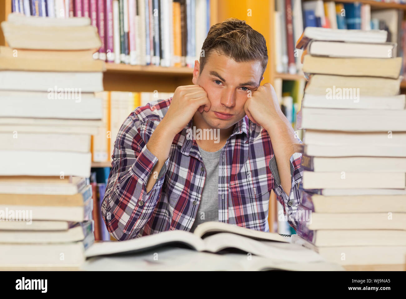 Irritated handsome student studying between piles of books in library ...