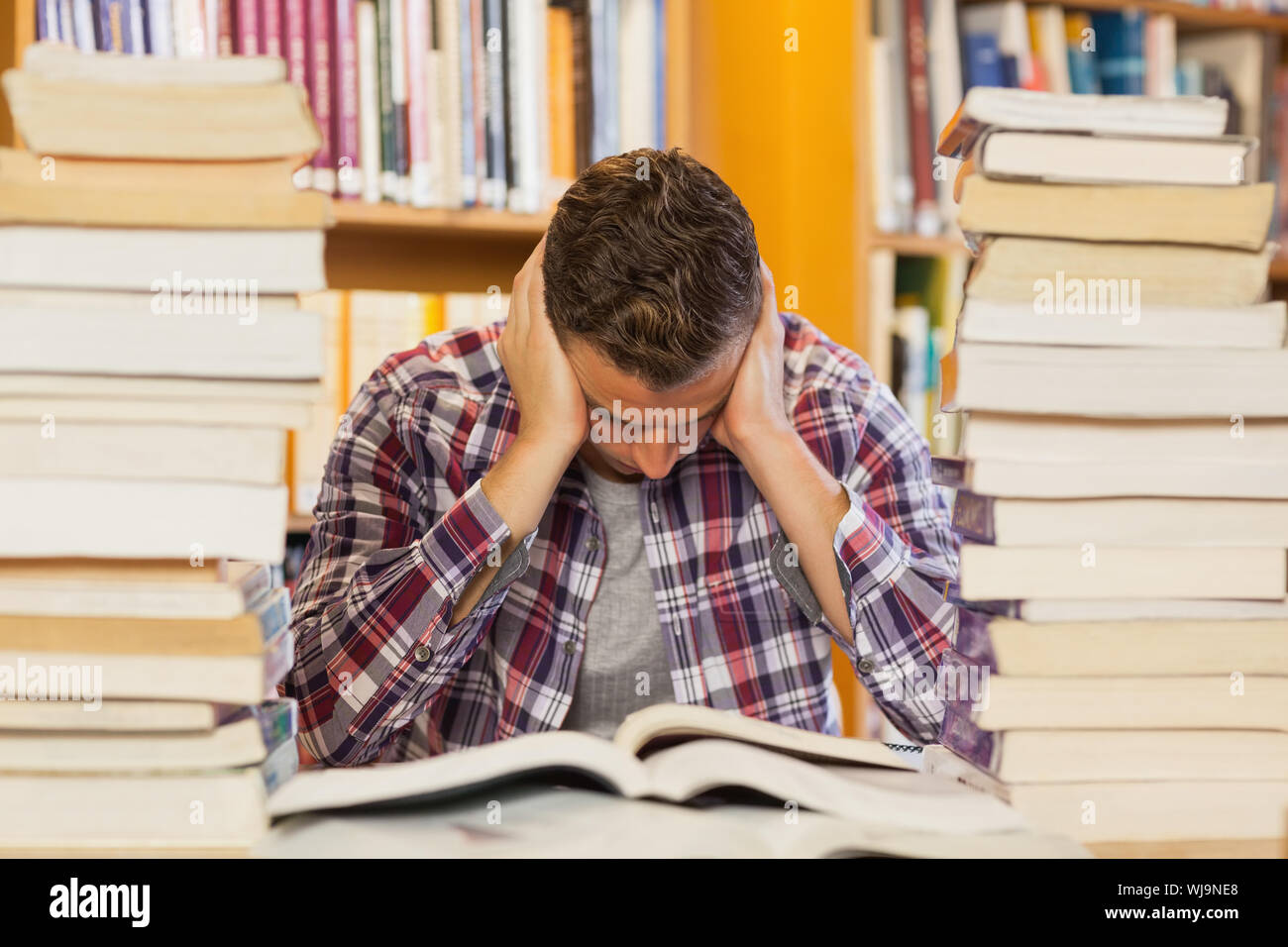 Concentrated handsome student studying between piles of books in ...