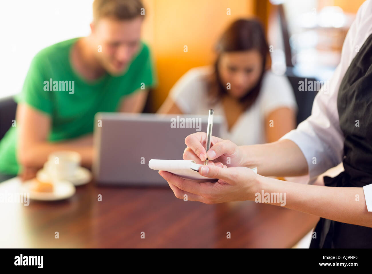 Close-up mid section of a waitress writing an order with two students ...