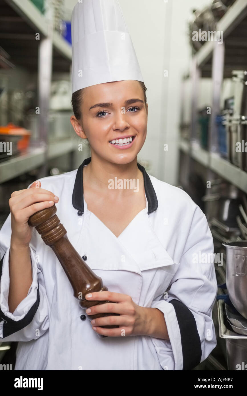 Young cheerful chef holding pepper mill between shelves in professional ...