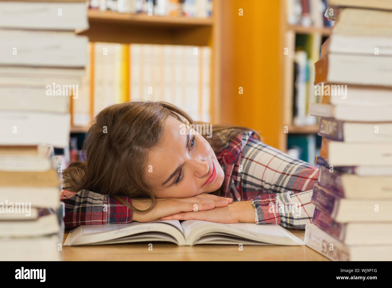 Tired pretty student resting head on table between piles of books in ...