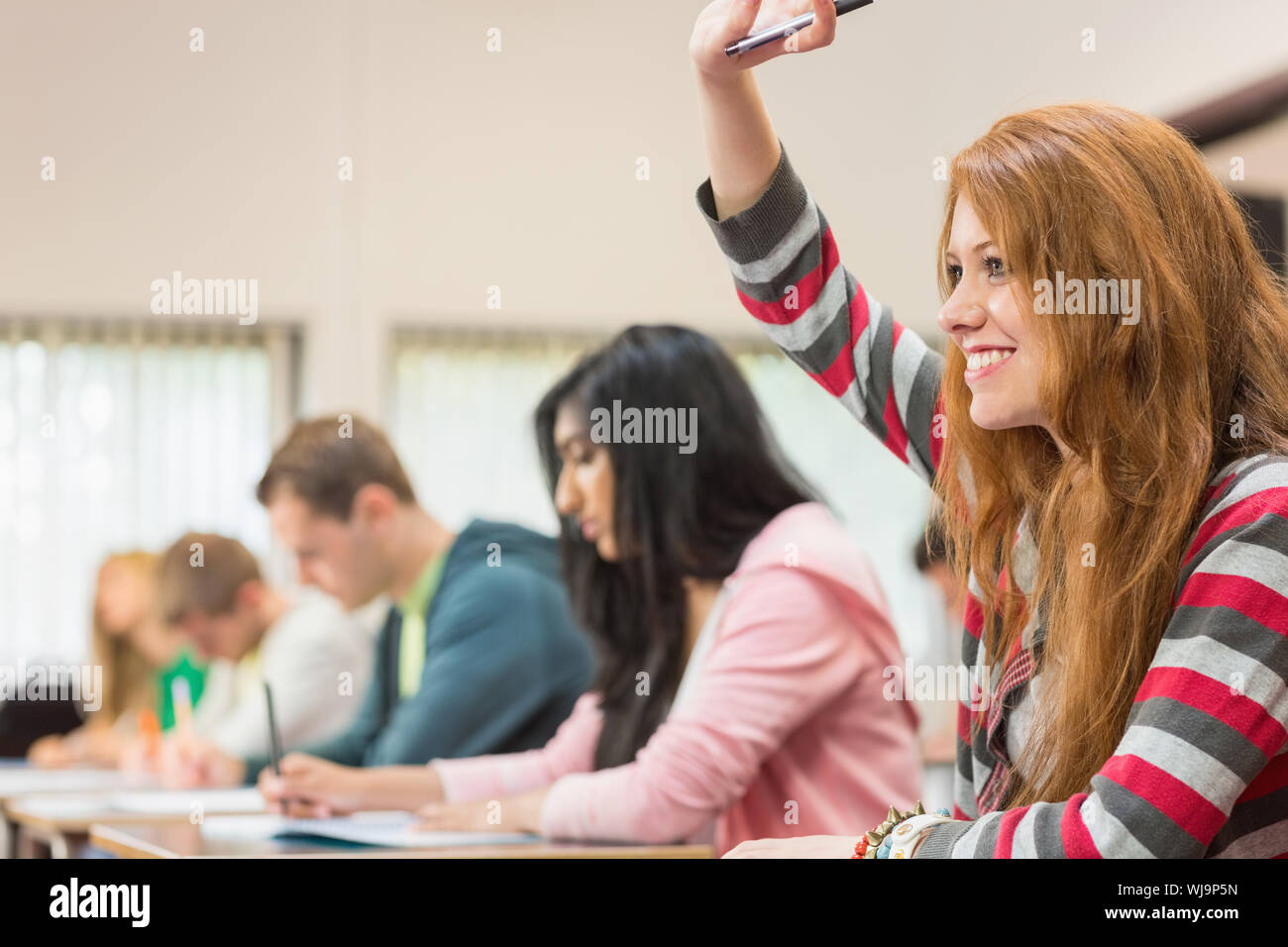 Side view of a young female student raising hand by others in the ...