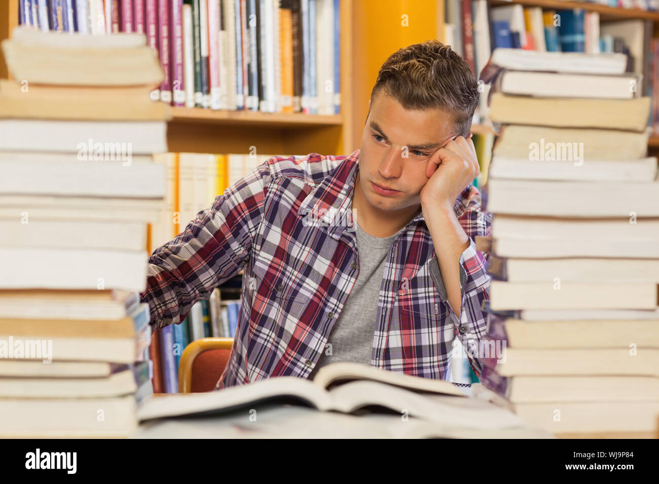 Frustrated handsome student studying between piles of books in library ...