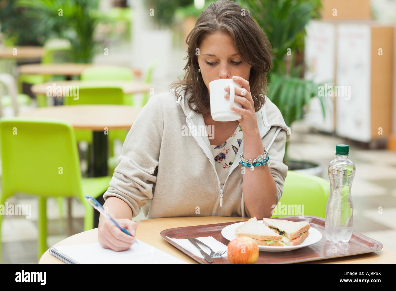 Female student doing homework while having breakfast in the cafeteria ...