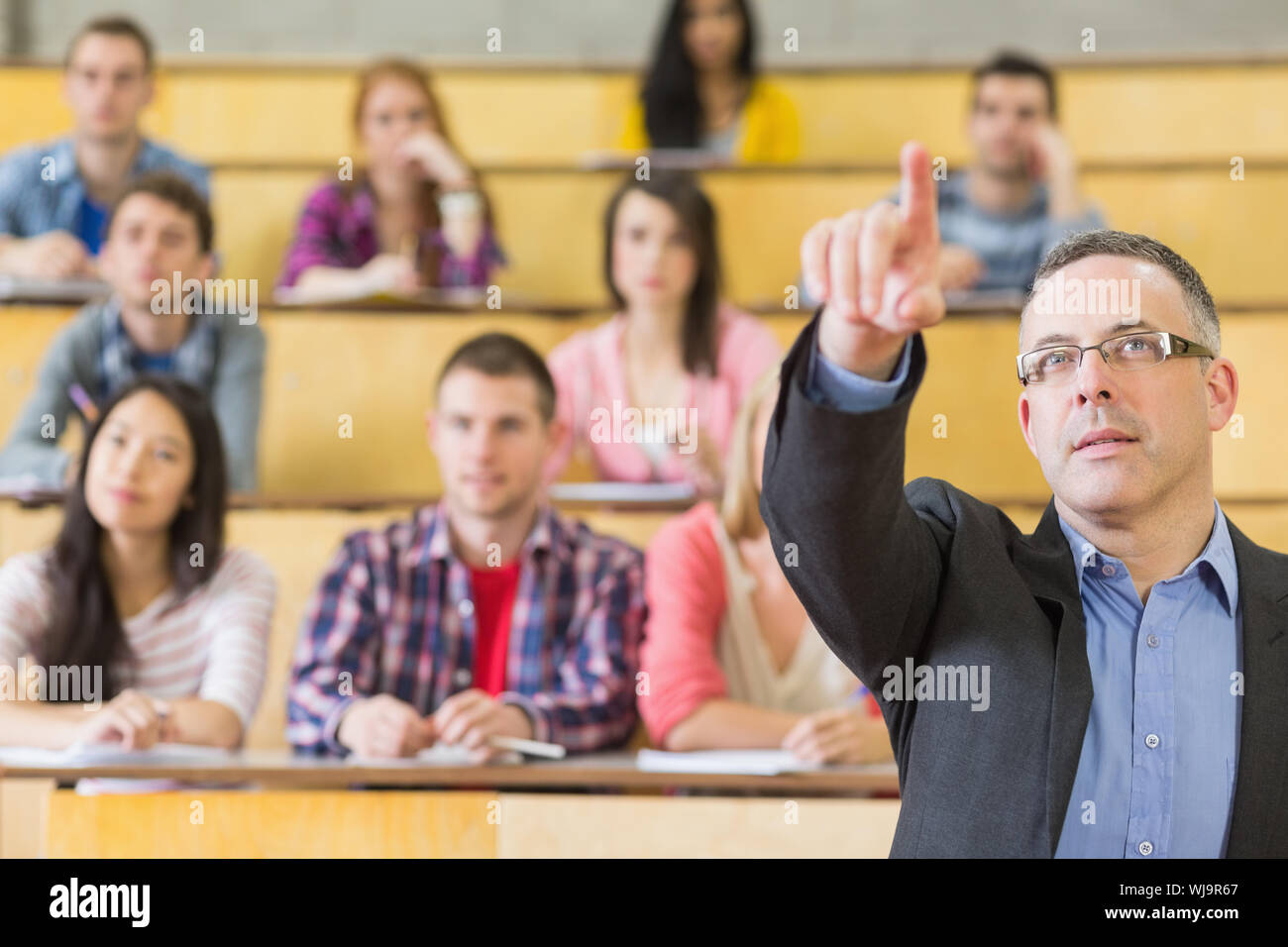 Elegant teacher pointing away with students sitting at the college ...