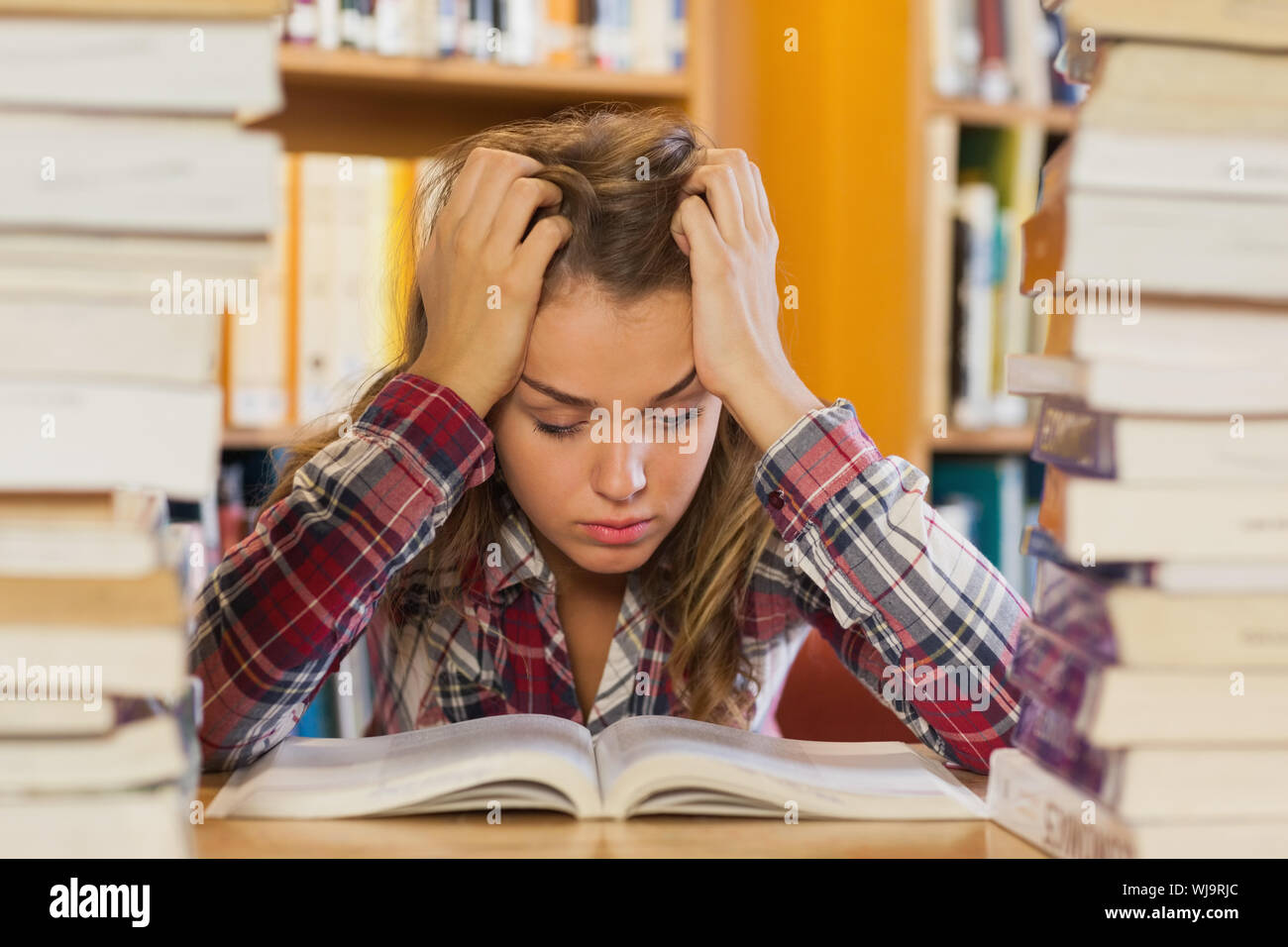 Irritated pretty student studying between piles of books in library ...