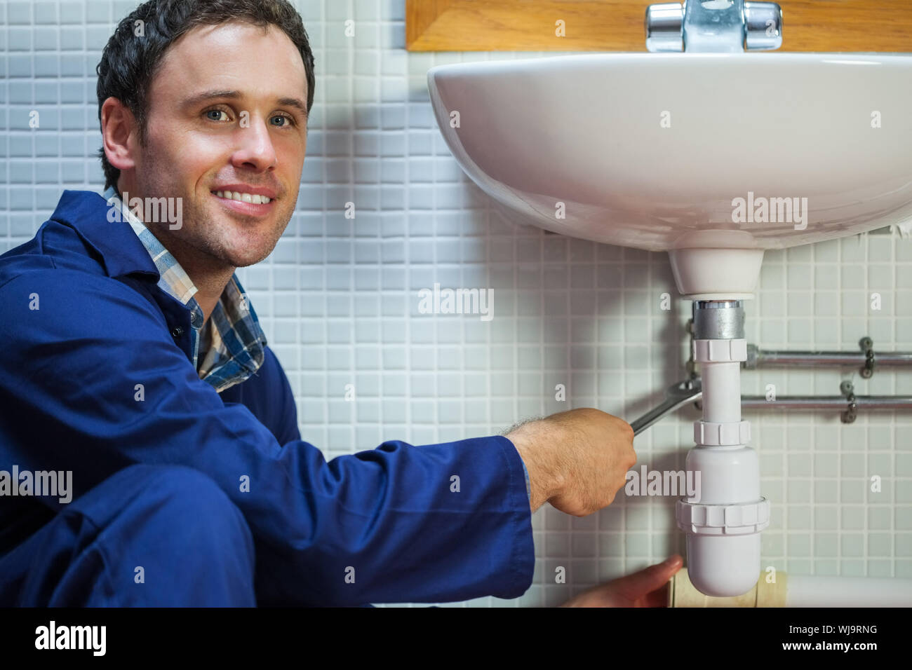 Handsome smiling plumber repairing sink in public bathroom Stock Photo ...