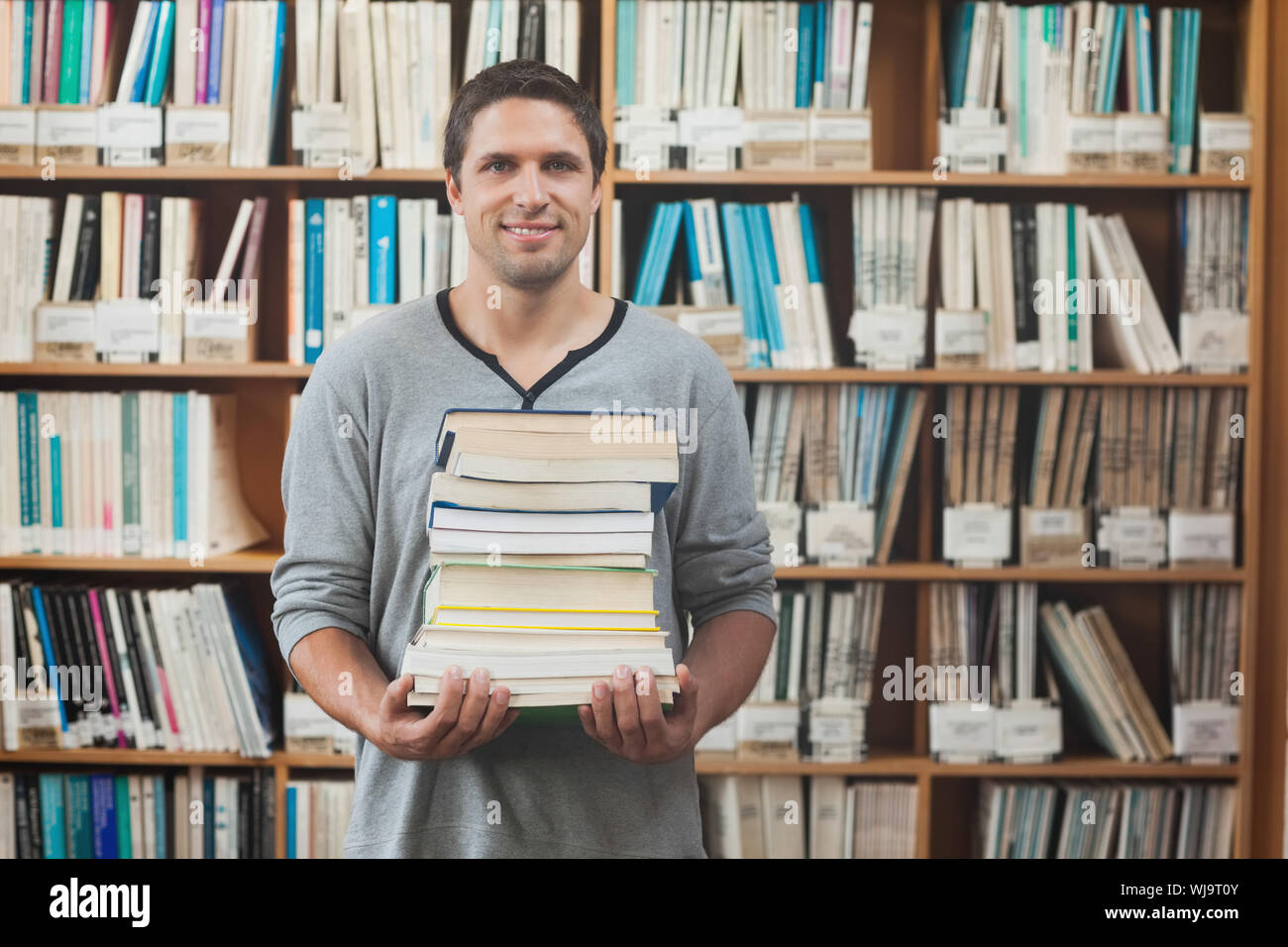 Attractive librarian holding a pile of books standing in library ...