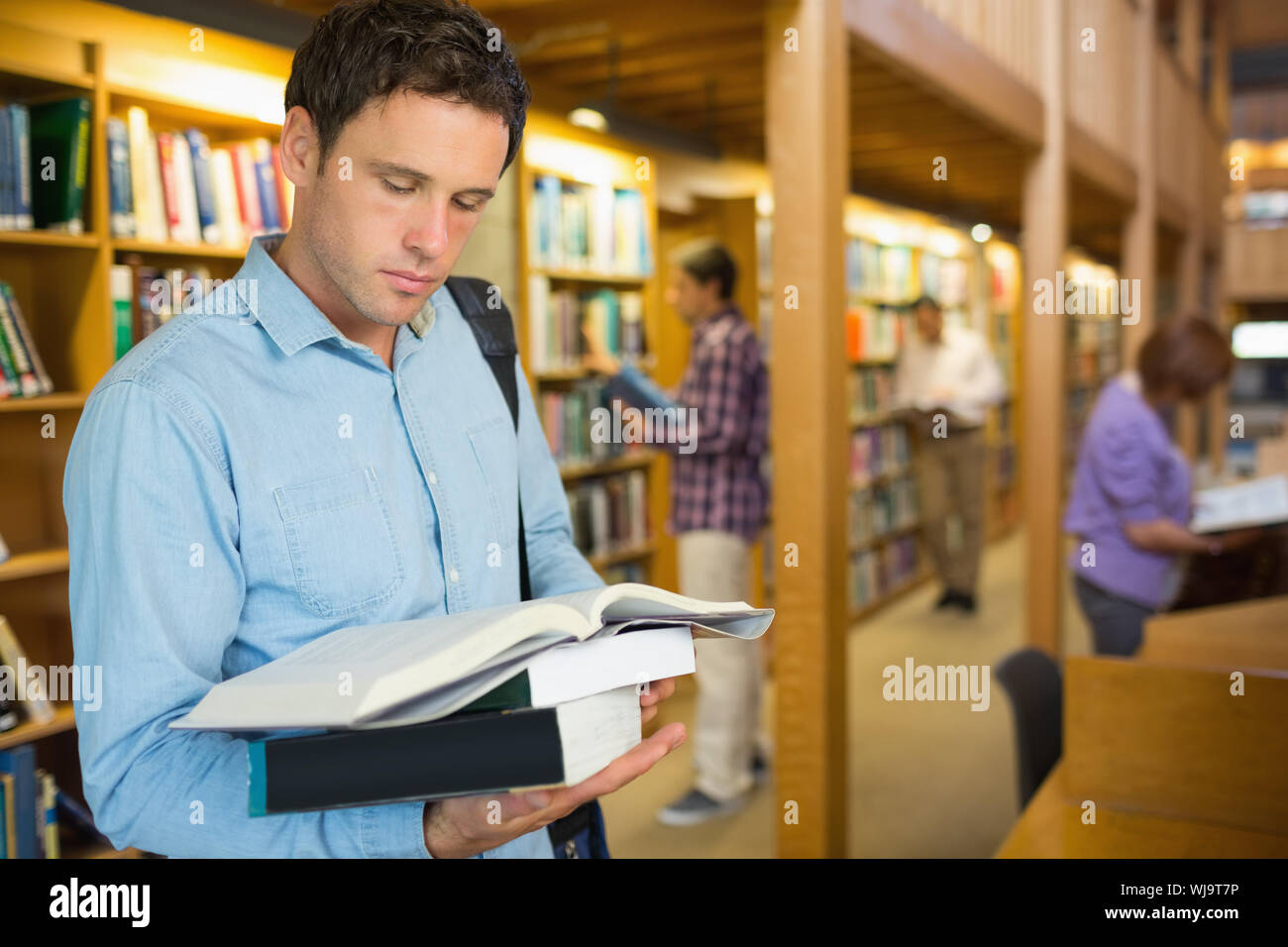 Serious mature student reading book with people in the background in ...