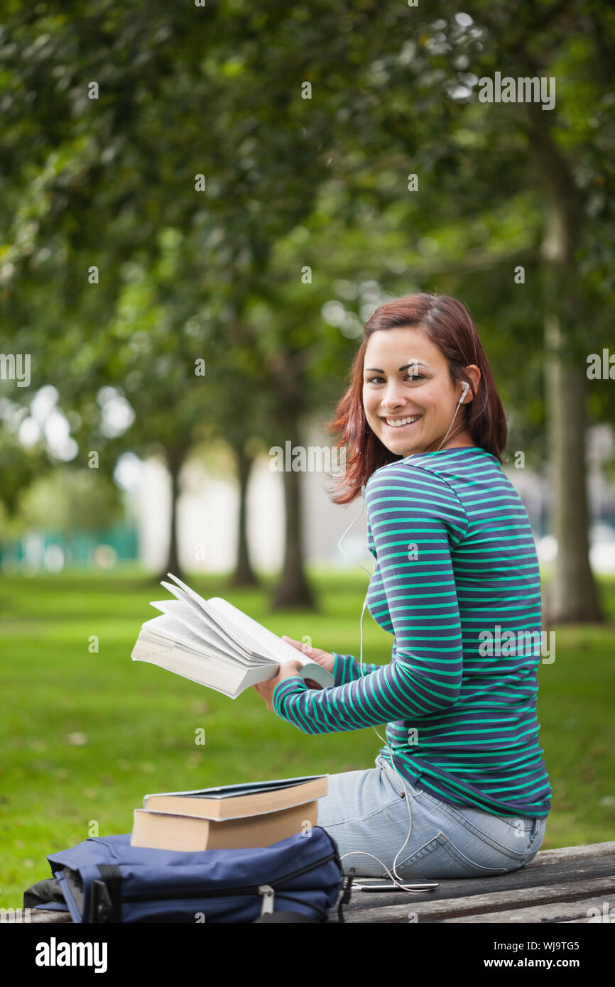 Happy casual student sitting on bench reading on campus at college ...
