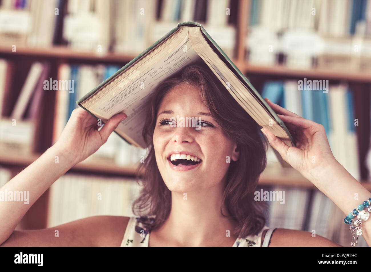 Close-up of a cheerful female student holding book over her head in the ...