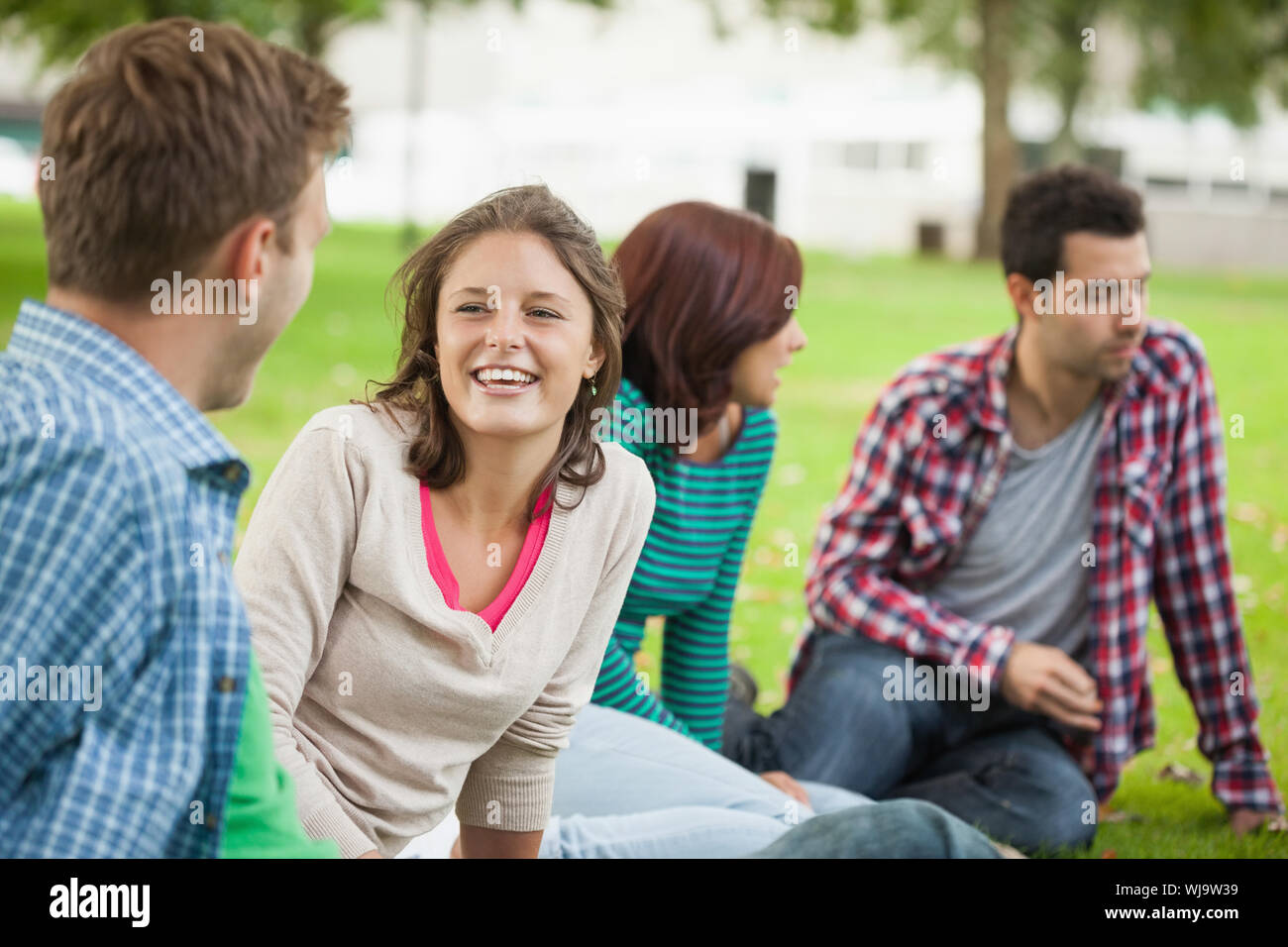 Casual laughing students sitting on the grass chatting on campus at ...