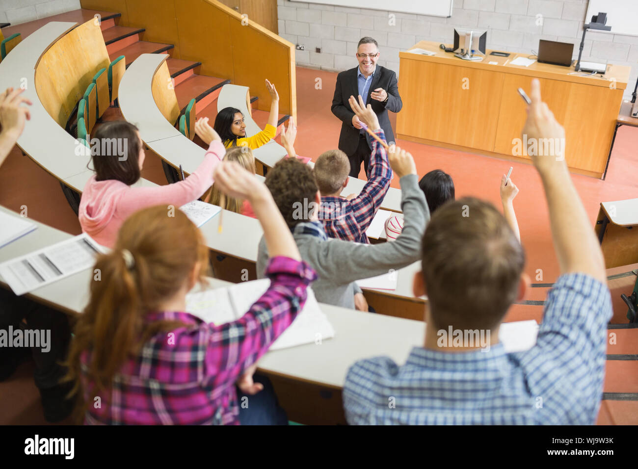 Rear view of students raising hands with a teacher in the college ...