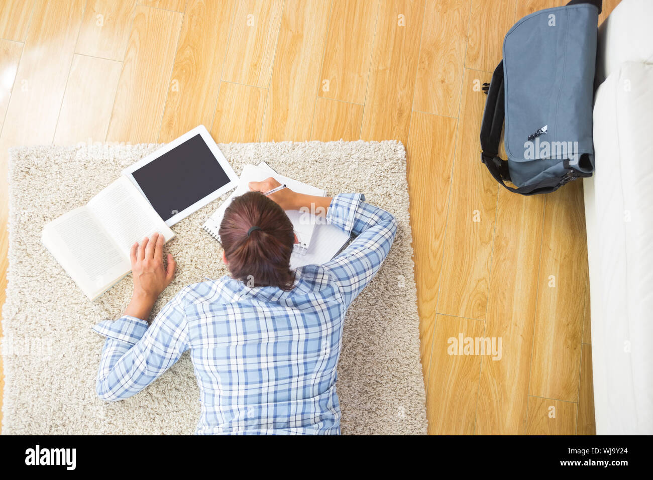 Young female student doing assignments while using her tablet and lying ...